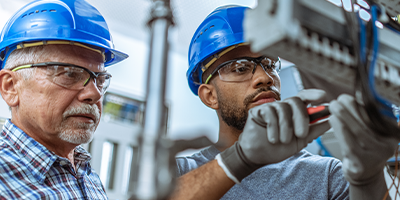two men wearing safety hats and gloves working on electrical